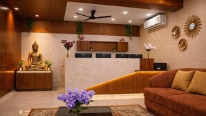 Um interior moderno com um balcão de receção em madeira, um sofá, uma estátua de Buda e elementos decorativos na parede.