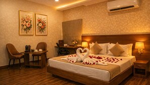 Quarto de hotel com uma cama, duas cadeiras, uma escrivaninha, um ventilador de teto, ar condicionado e dois quadros decorativos com flores.