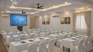 Uma sala de conferências com mesas, cadeiras, tela de projetor e aparelhos de ar condicionado.