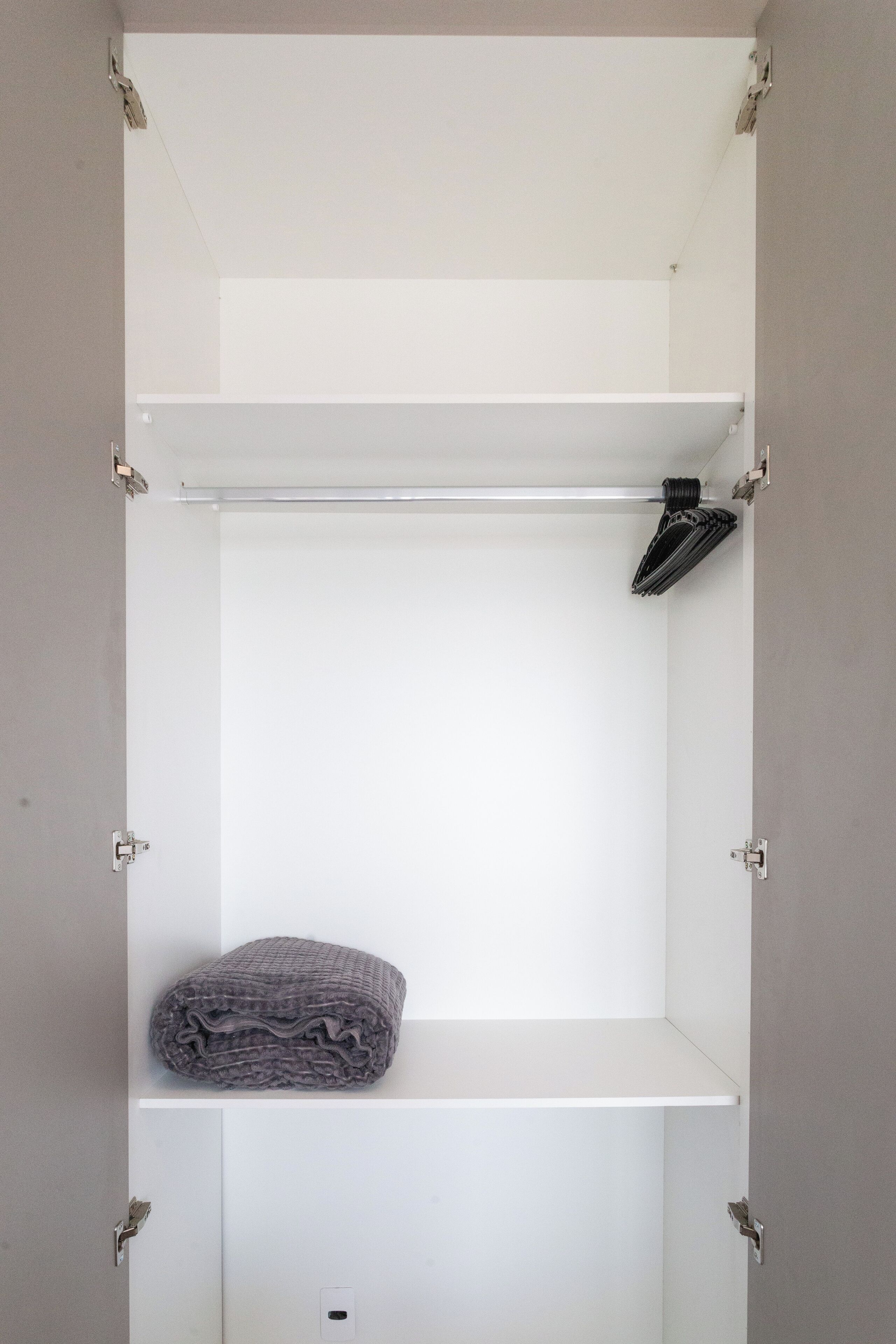 Um armário branco com três prateleiras, uma barra para pendurar roupas e uma toalha dobrada.