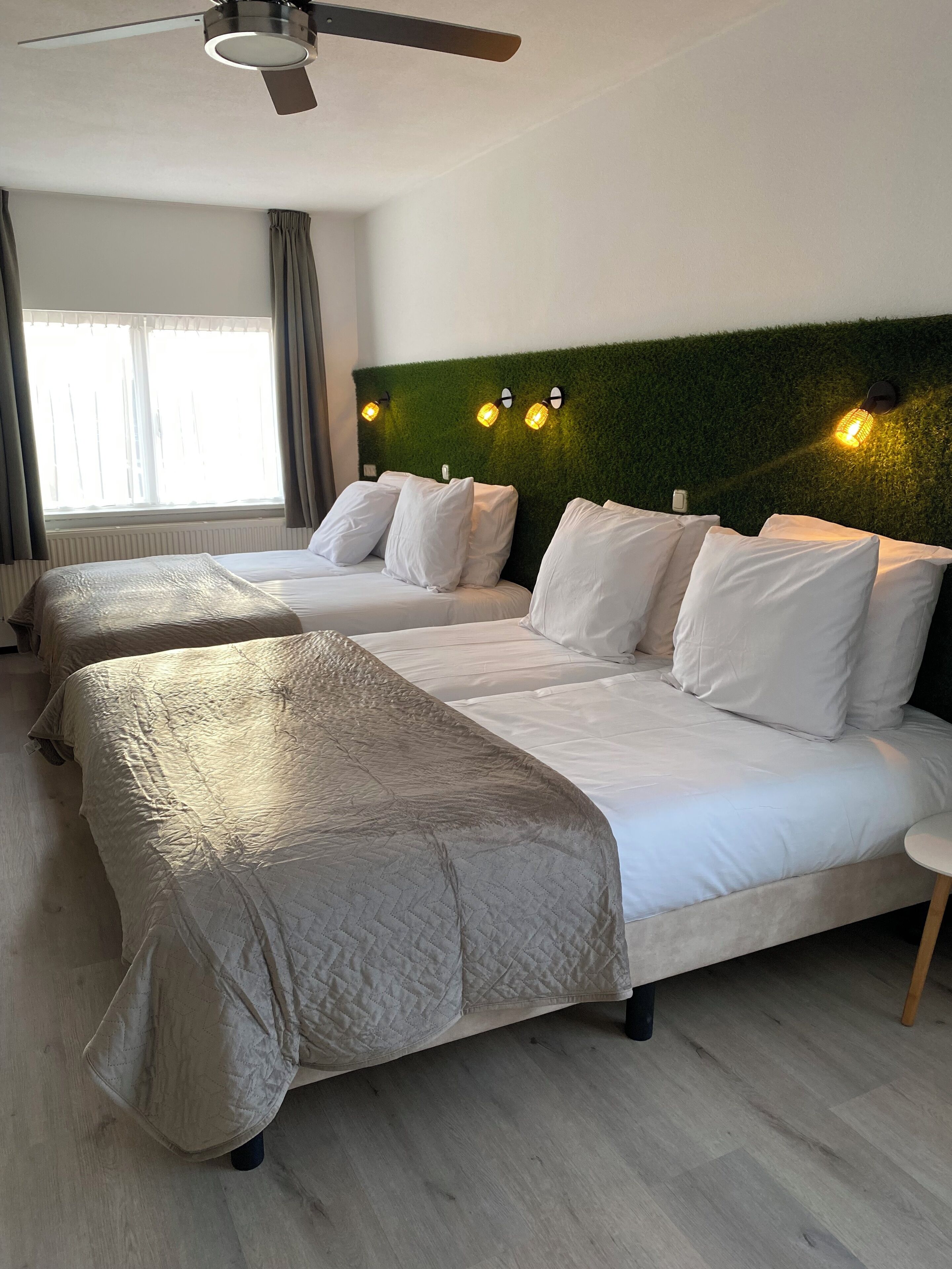 Quarto de hotel com duas camas, um ventilador de teto e uma parede verde com luzes fixadas.