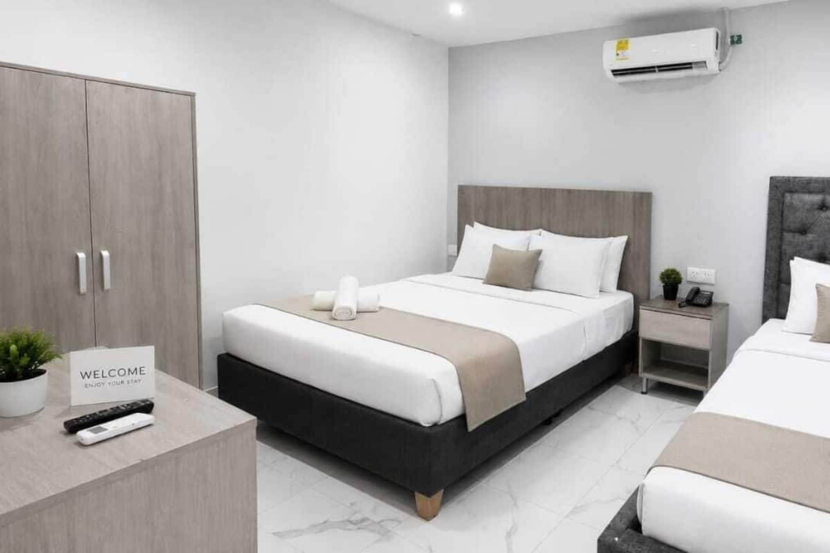 Quarto de hotel moderno com duas camas, um guarda-roupa, mesa de cabeceira com telefone e placa de boas-vindas.
