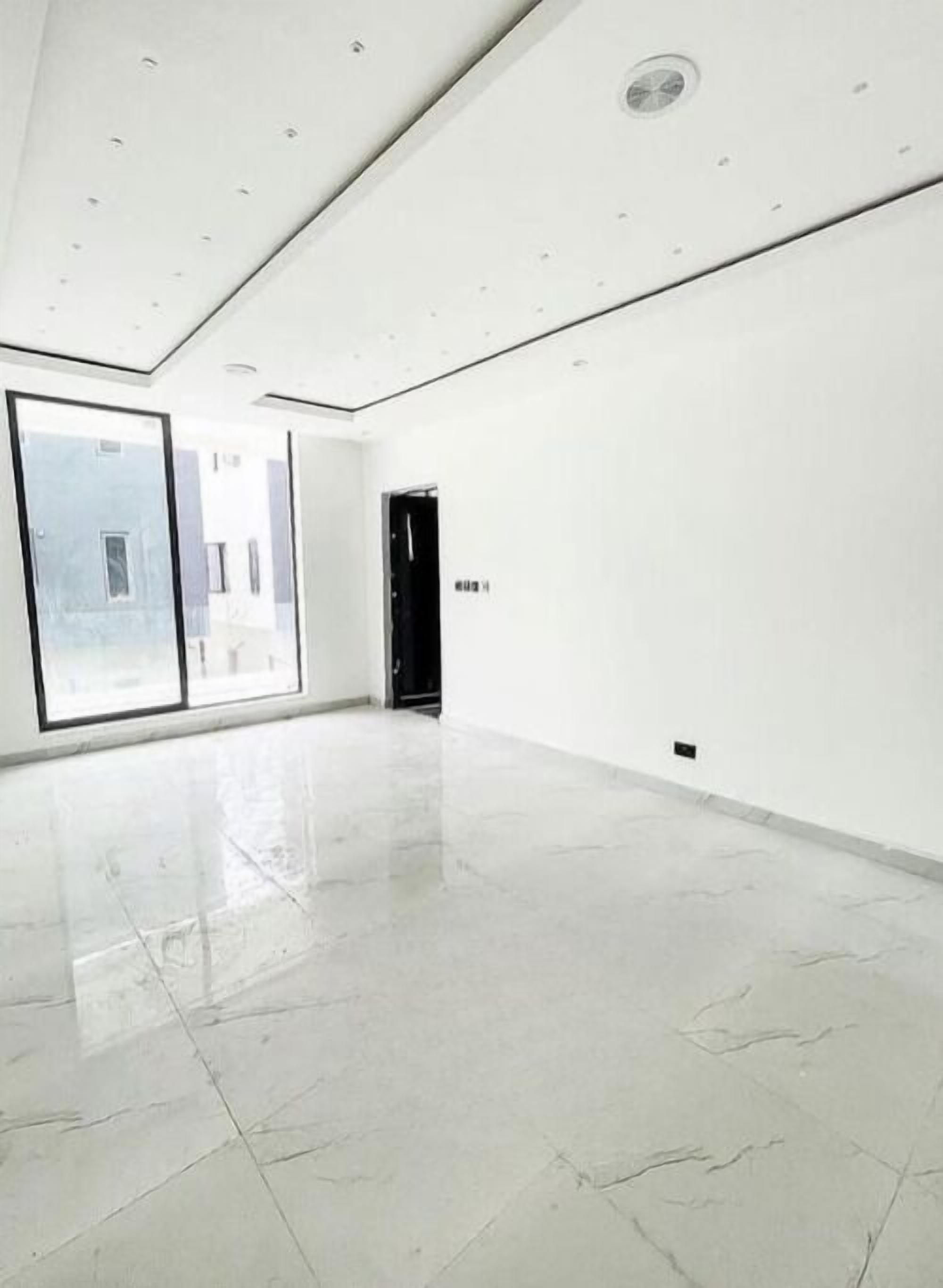 Um quarto amplo e vazio, com uma janela grande, uma porta e piso de azulejos.