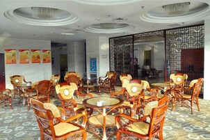 Um hall de hotel com mesas redondas e cadeiras de vime, um tapete estampado e um teto decorativo.