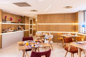 Uma sala de jantar moderna com mesas e cadeiras de madeira, opções de café da manhã e um ambiente claro e bem iluminado.