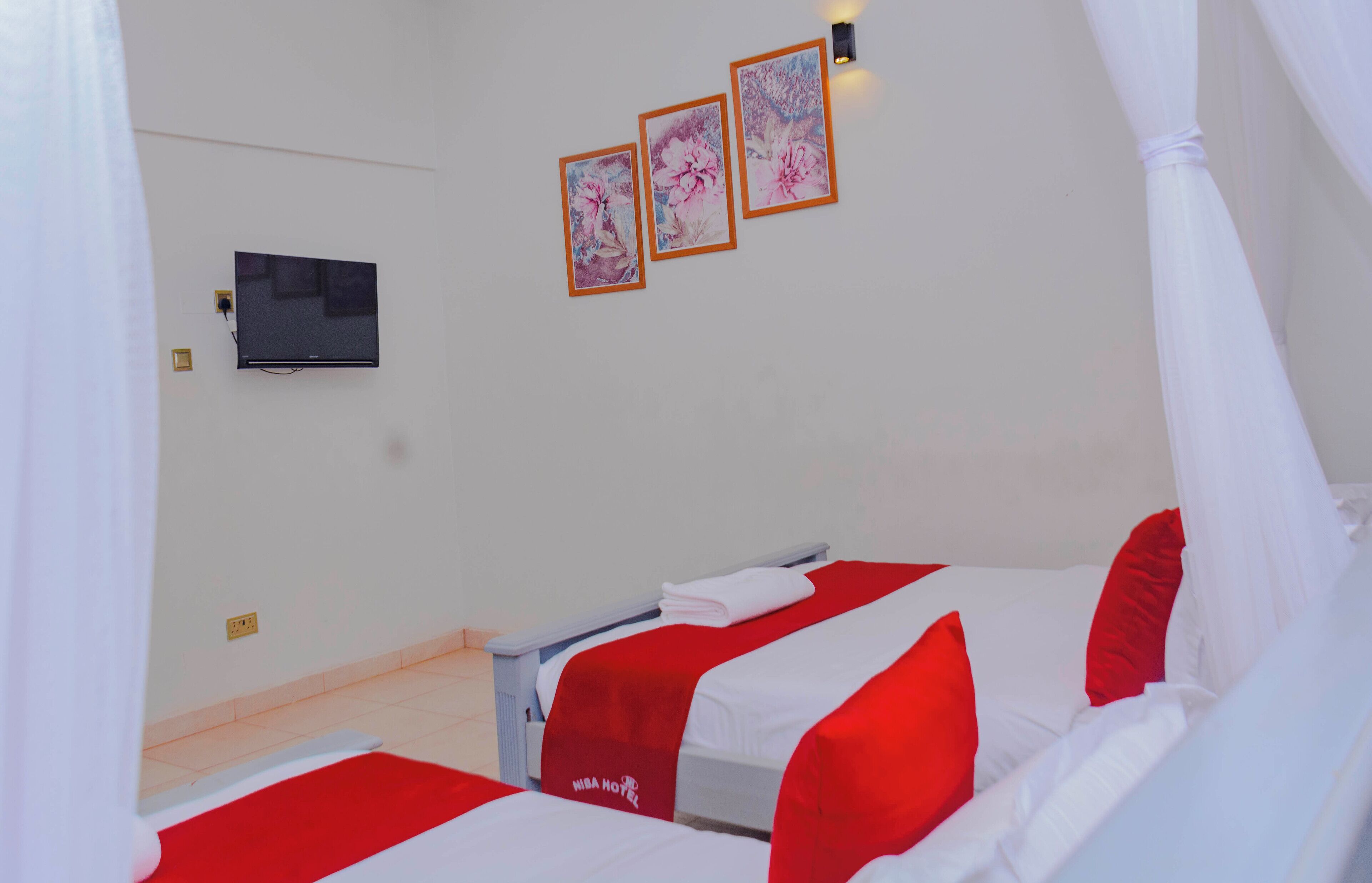 Quarto de hotel com duas camas, uma televisão e três quadros na parede.