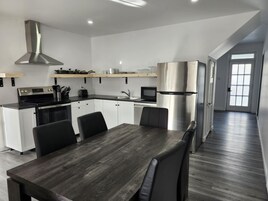 Uma cozinha moderna com ilha central, eletrodomésticos de aço inoxidável e área de jantar com mesa e cadeiras de madeira escura.
