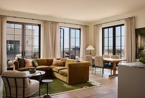 Uma sala de estar moderna com sofá, poltronas, uma mesa de jantar e grandes janelas.
