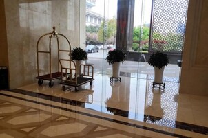 Um hall com piso lustroso, um carrinho de metal e plantas em vasos.