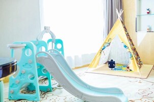 Espaço infantil com escorrega, tenda de brincar e uma mesa com brinquedos.