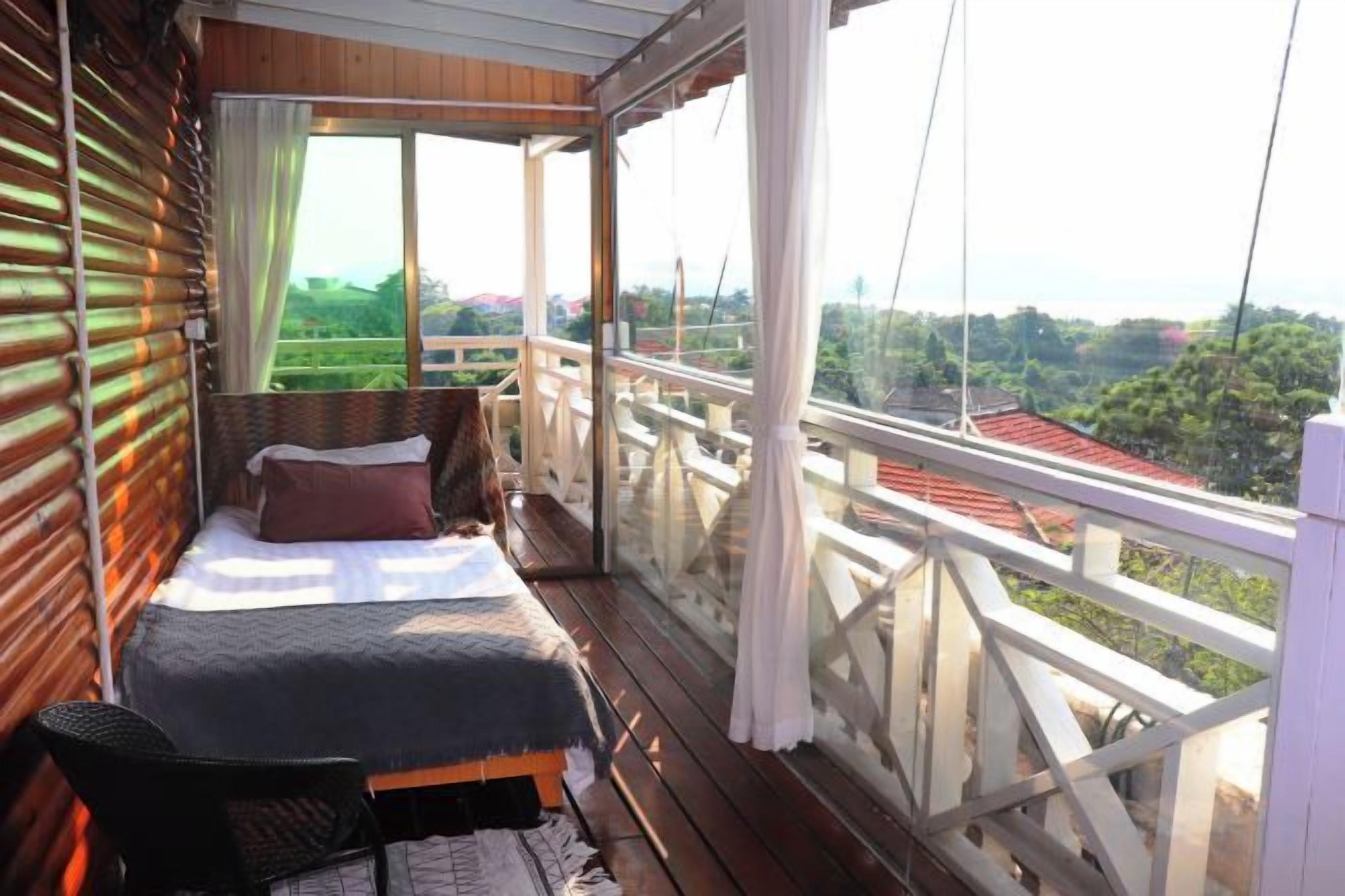 Uma varanda com cama, cadeira e vista para o verde.