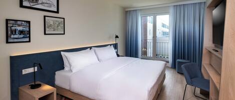 Quarto de hotel moderno com uma cama grande, uma escrivaninha com abajur, televisão e quadros na parede.