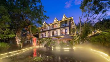 Um edifício em estilo tradicional com um lago refletor na frente, rodeado por vegetação exuberante.