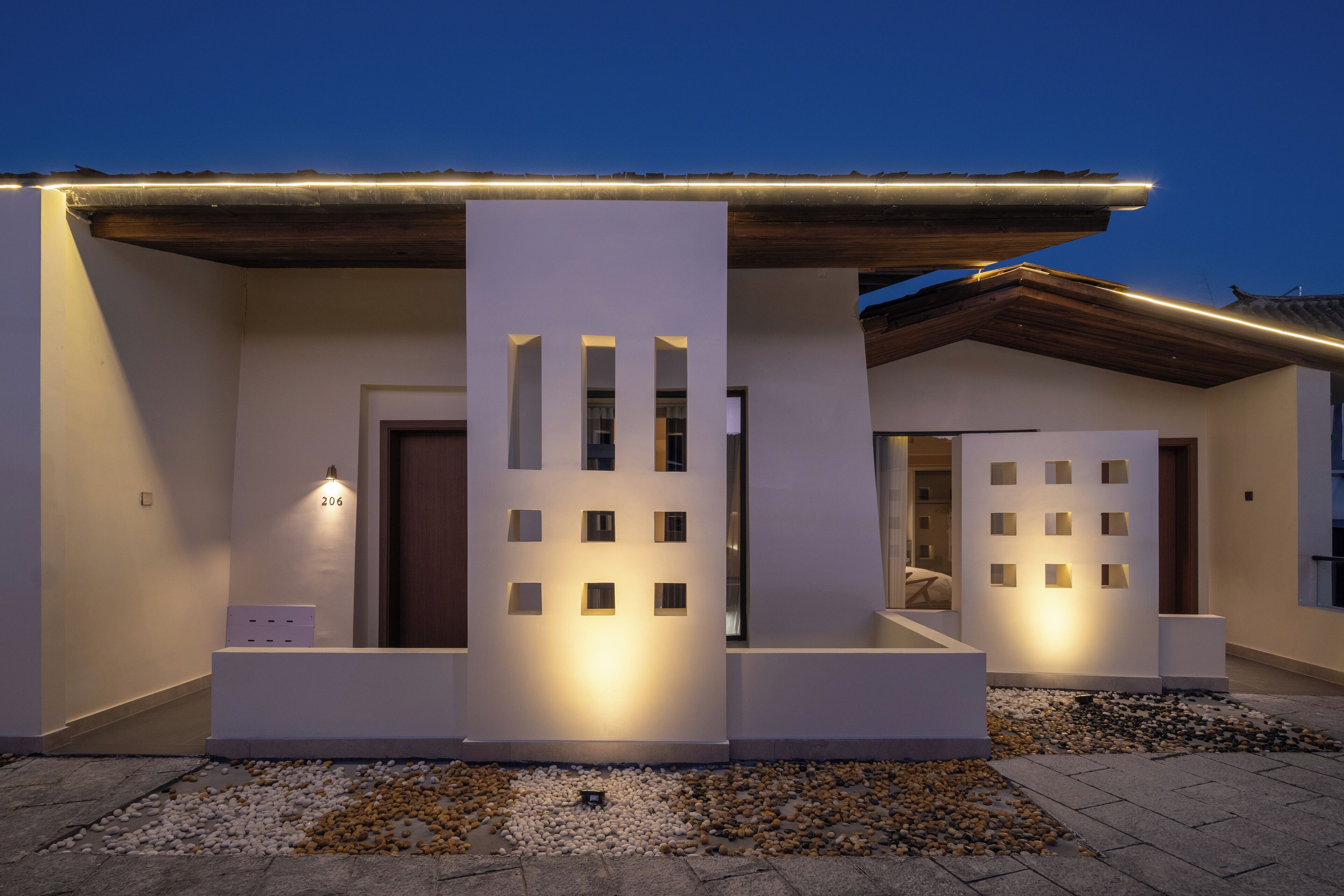 Um edifício moderno com telhado plano, estrutura de vigas de madeira e uma série de painéis iluminados na fachada.