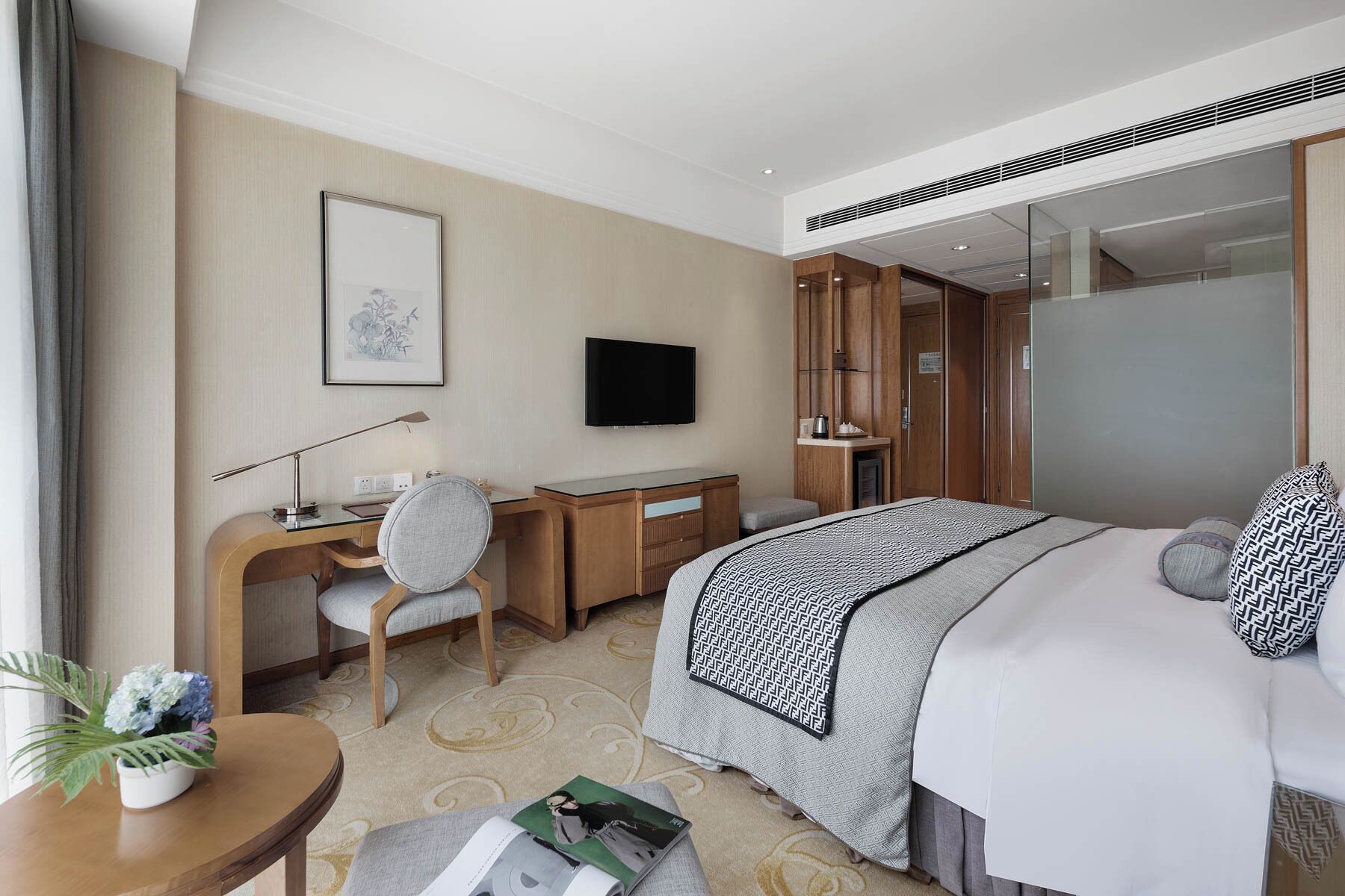 Quarto de hotel com cama, escrivaninha, cadeira, televisão e guarda-roupa.