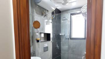 Casa de banho moderna com cabine de chuveiro em vidro, lavatório branco e ventoinha no teto.