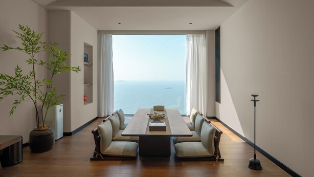 Uma sala de jantar com vista para o mar, um vaso de planta e uma luminária de chão moderna.