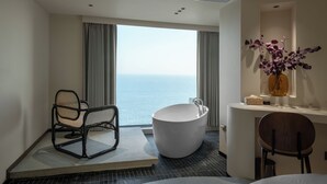 Uma casa de banho moderna com uma banheira grande, uma cadeira e vista para o mar.