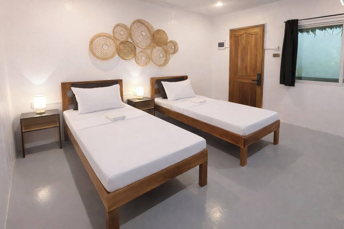 Quarto com duas camas de madeira, um cesto decorativo fixado na parede, uma porta de madeira e uma janela com cortinas.