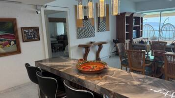 Cozinha moderna com bancada de mármore, banquetas pretas, luminárias pendentes e vista para o oceano.