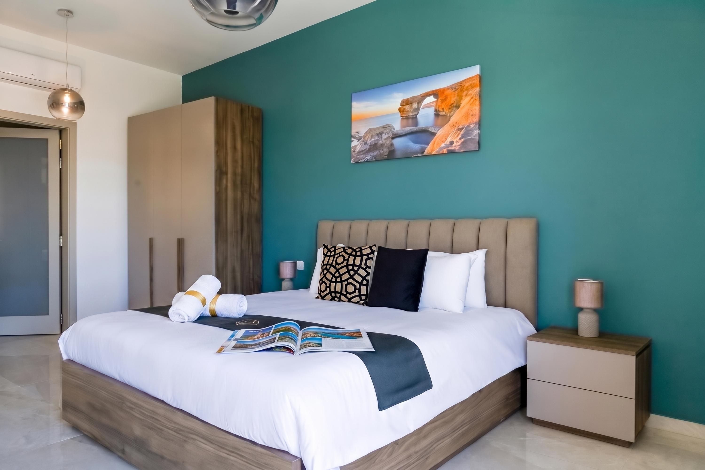 Quarto de hotel moderno com uma cama grande, mesa de cabeceira, guarda-roupa e um quadro na parede.