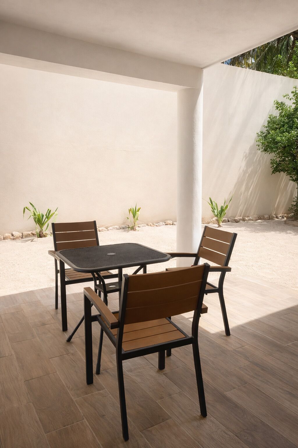 Pátio externo com mesa e quatro cadeiras, cercado por um muro baixo e pequenas plantas.
