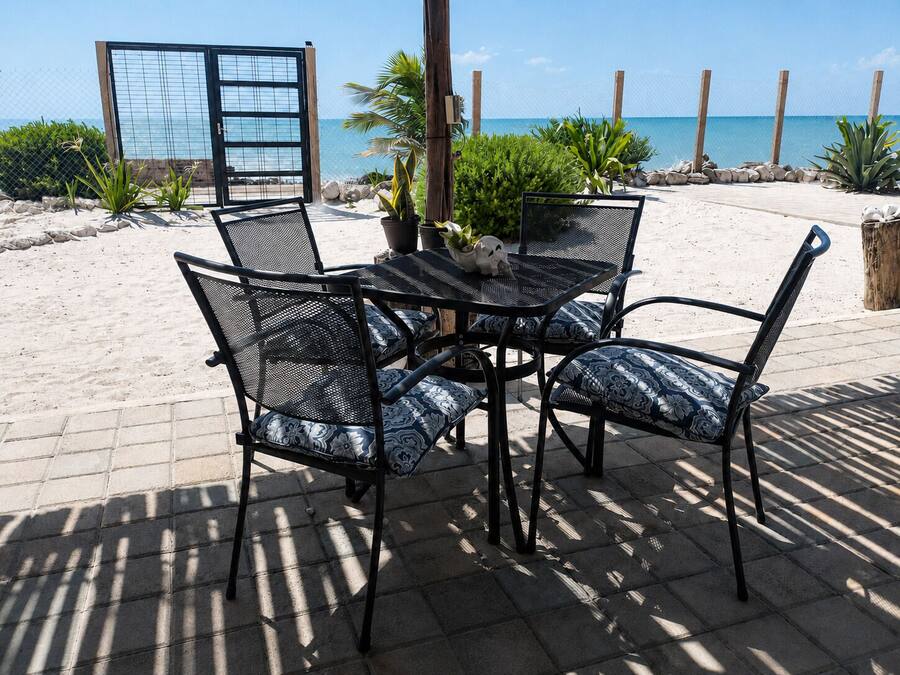 Um pátio com mesa e cadeiras, vista para a praia e um cercado.
