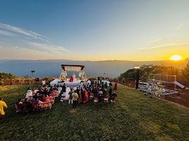 Uma cerimônia de casamento em uma colina gramada, com vista desobstruída para o pôr do sol e montanhas ao longe.
