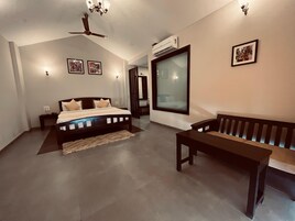 Quarto com cama, um banquinho, ventoinha no teto e uma janela grande.