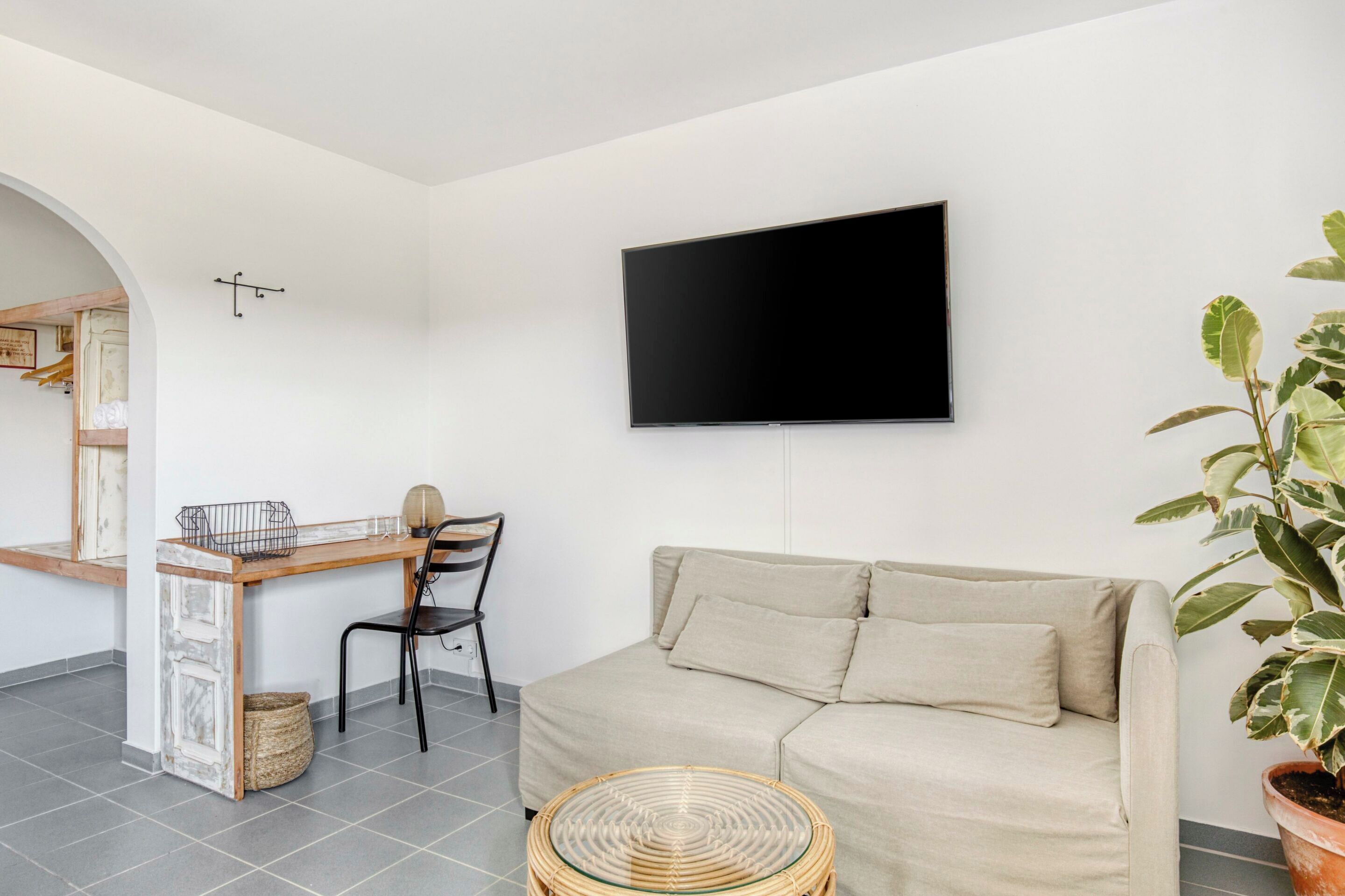 Uma sala de estar moderna com televisão de tela plana, sofá, poltrona, mesinha e planta em vaso.