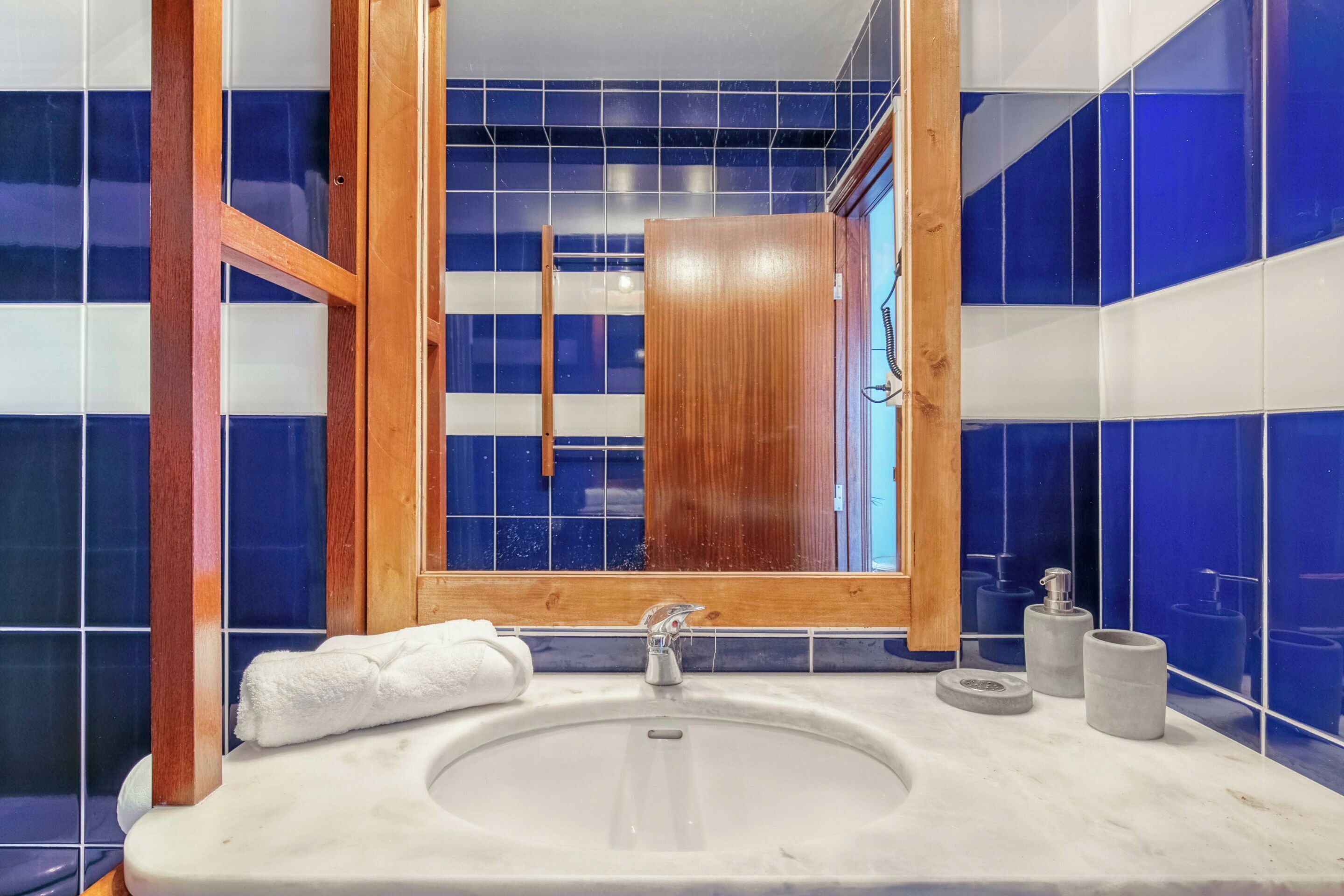 Casa de banho com um espelho grande, uma pia e azulejos azuis.