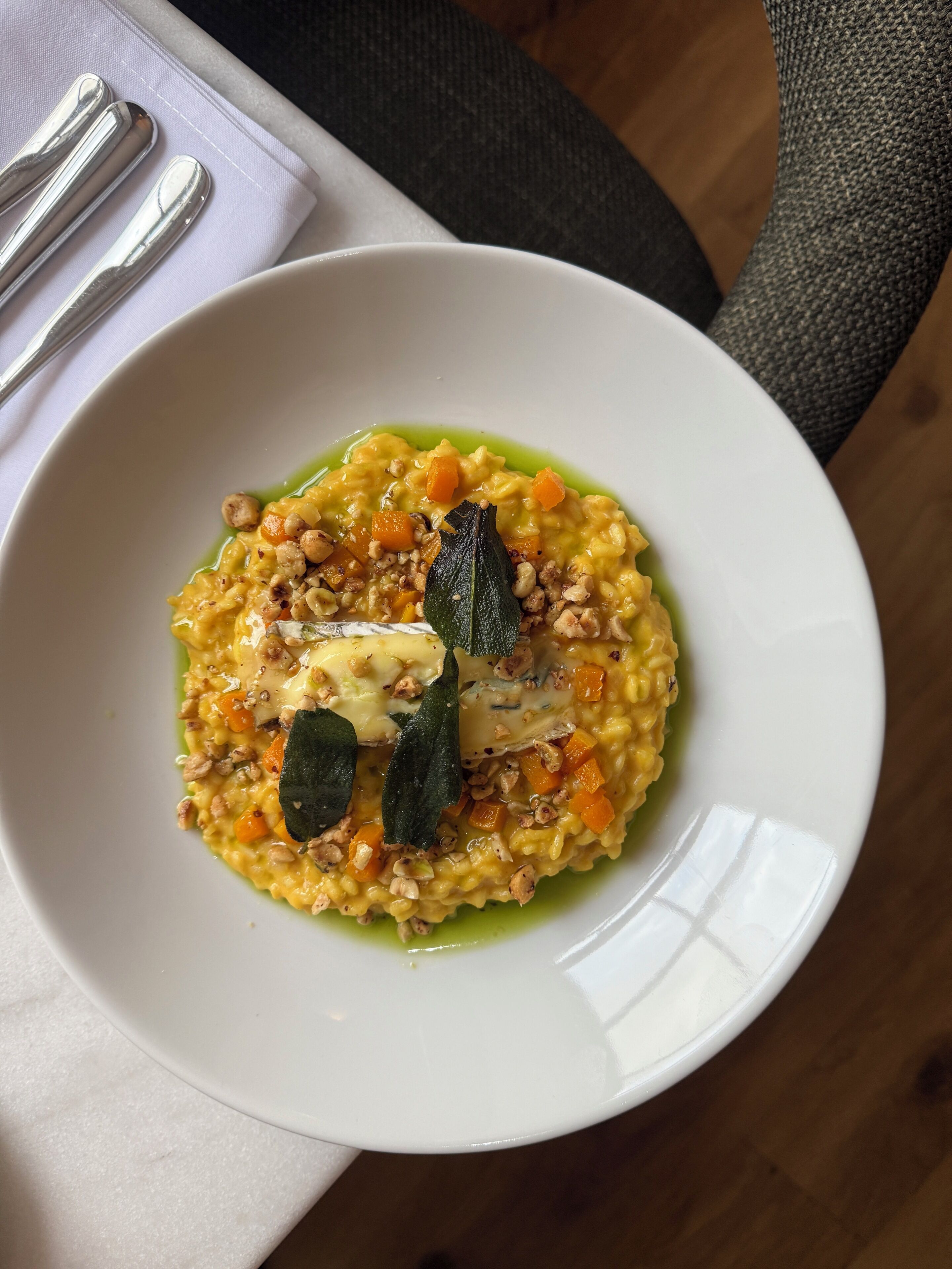 Uma tigela branca com comida e molho verde, colocada sobre uma mesa com um guardanapo e talheres.
