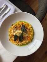 Uma tigela branca com comida e molho verde, colocada sobre uma mesa com um guardanapo e talheres.
