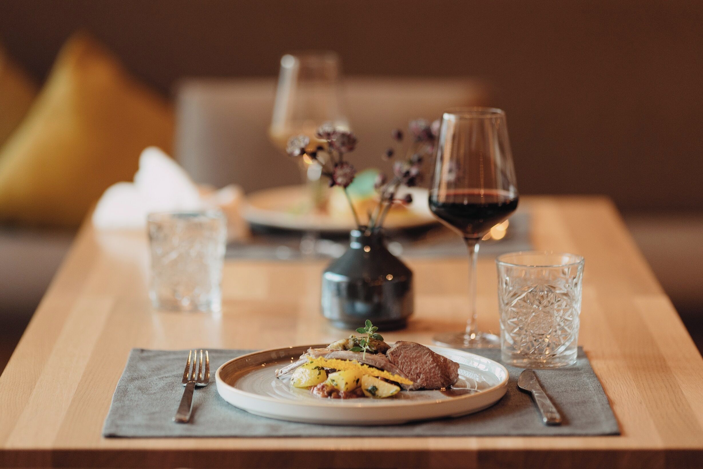 Uma mesa de jantar com um prato de comida, um copo de vinho tinto e um vaso com flores.
