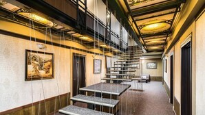 Um amplo hall de hotel com teto alto, escadaria e diversas áreas de estar.