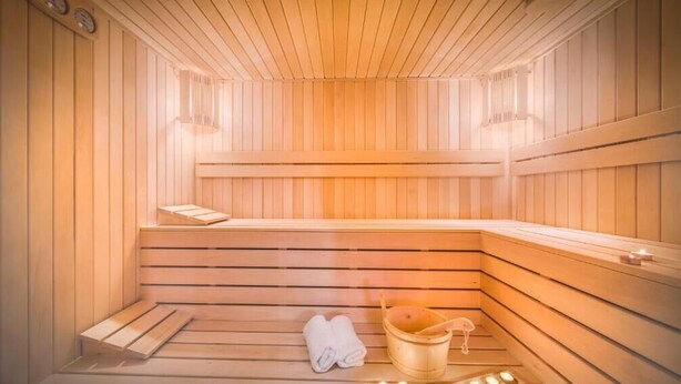 Uma sauna de madeira com bancos, um porta-toalhas, um balde e velas.