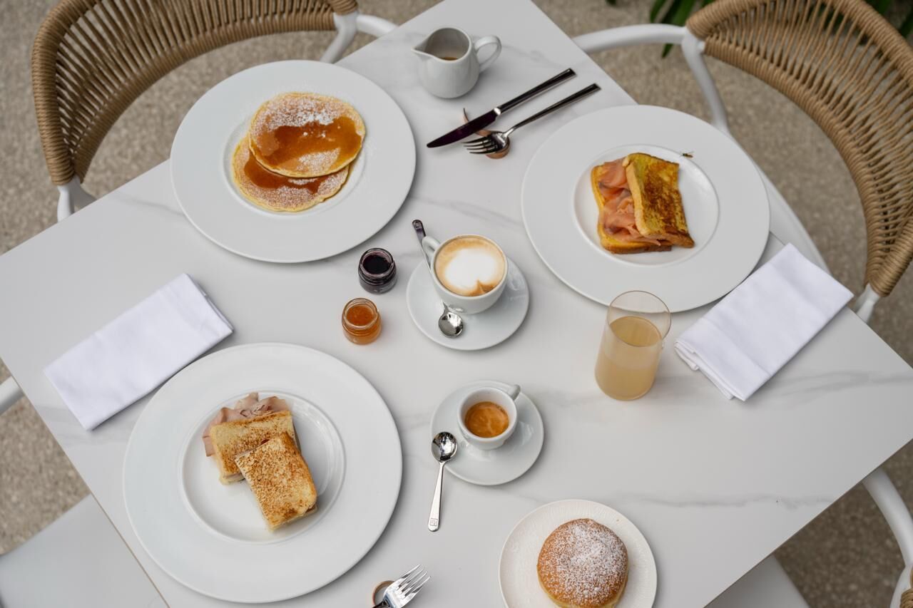 Uma mesa posta com pratos de comida, uma xícara de café e um copo de bebida transparente.