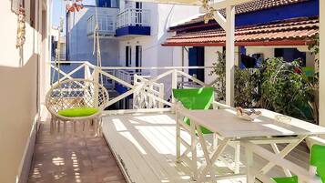 Uma varanda com guarda-corrimão branco, uma cadeira suspensa com almofada verde e uma mesa com cadeiras verdes.