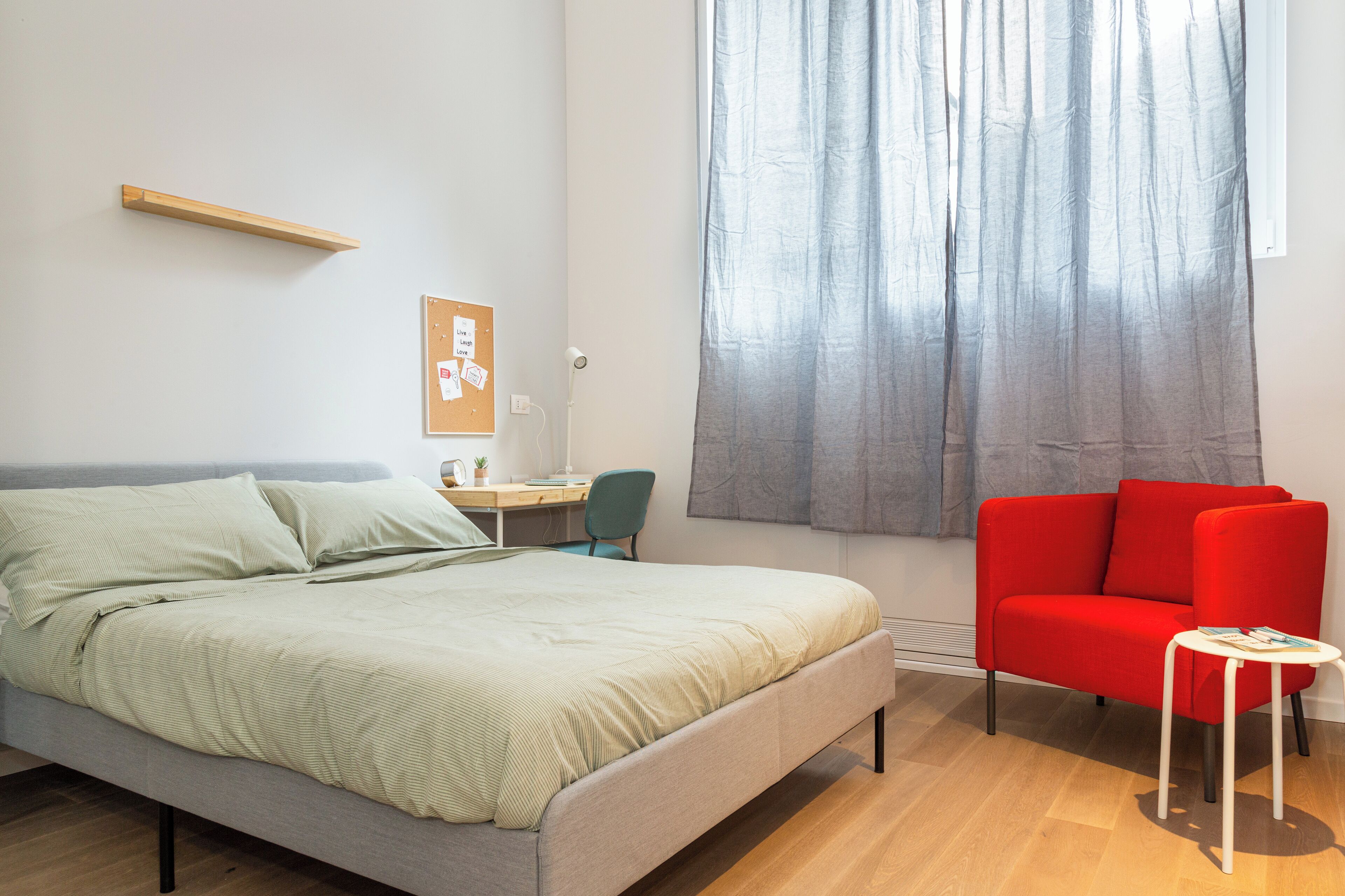 Quarto com uma cama, uma escrivaninha, uma cadeira e uma poltrona vermelha.