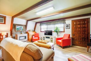Uma sala de estar acolhedora com lareira, uma televisão e duas poltronas vermelhas.