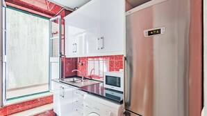 Uma cozinha compacta com máquina de lavar, micro-ondas e geladeira de aço inoxidável.