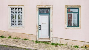 Um edifício com uma porta branca, uma janela com grade de metal e outra janela com moldura verde.