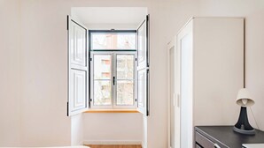 Quarto com cama, escrivaninha, luminária e janela com venezianas abertas.