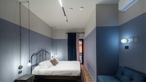 Quarto moderno com cama, mesa de cabeceira e um sofá azul.
