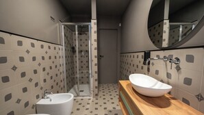 Casa de banho moderna com cabine de duche em vidro, bidé, lavatório com toucador em madeira e espelho sobre o lavatório.