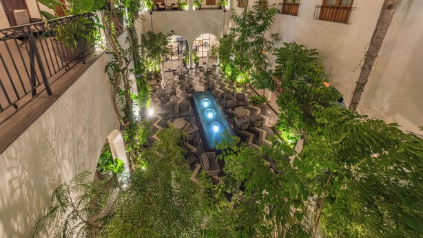 Um pátio com piscina central, rodeado por áreas de estar e vegetação exuberante.