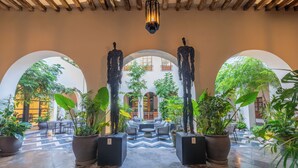 Um pátio interno amplo com área de estar central, rodeado por grandes vasos de plantas e arcos.