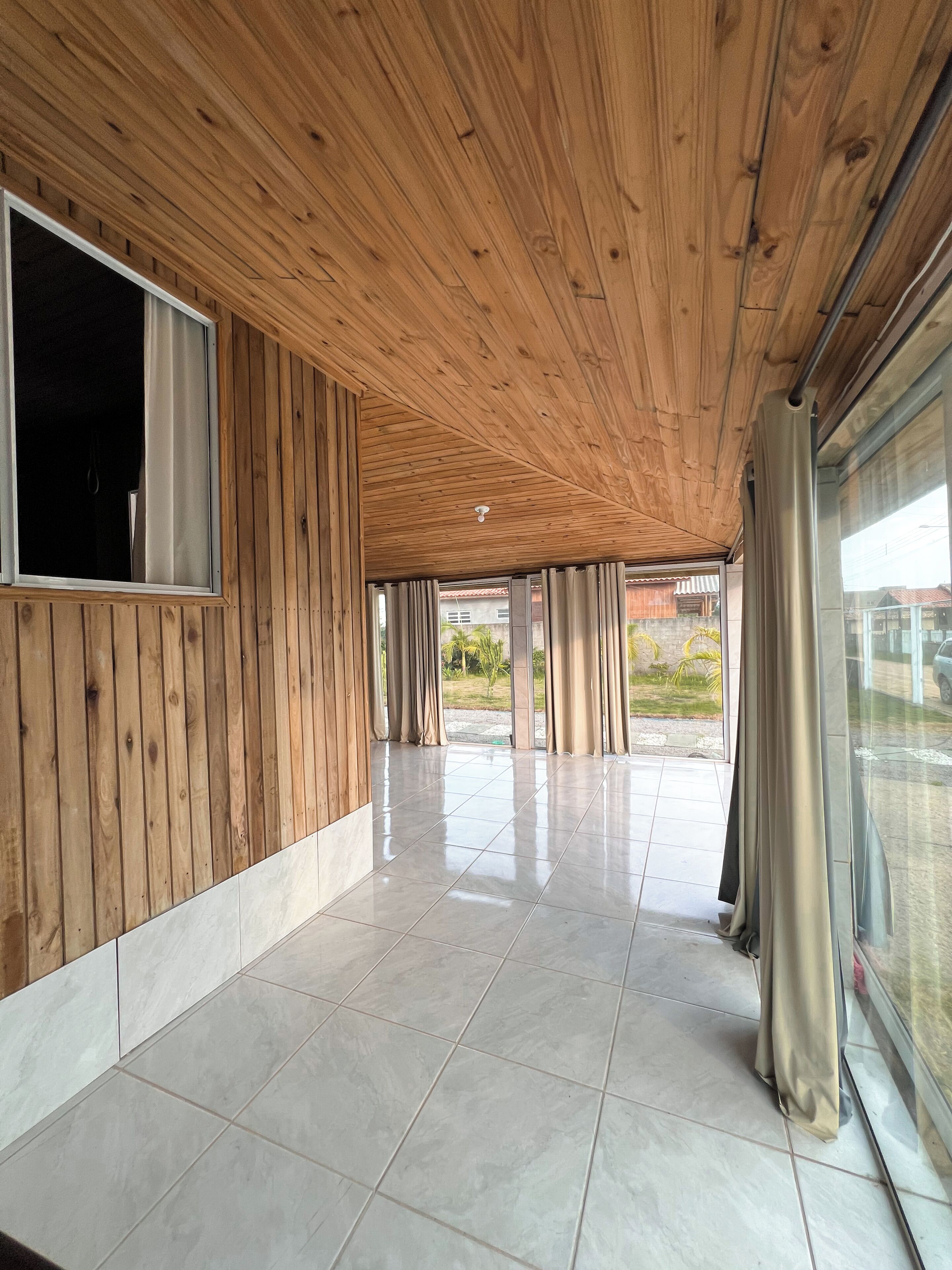 Um quarto espaçoso com teto de madeira, janelas amplas e piso de azulejos.