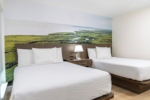 Quarto de hotel com duas camas, uma mesa de cabeceira com abajur e um grande mural de paisagem.