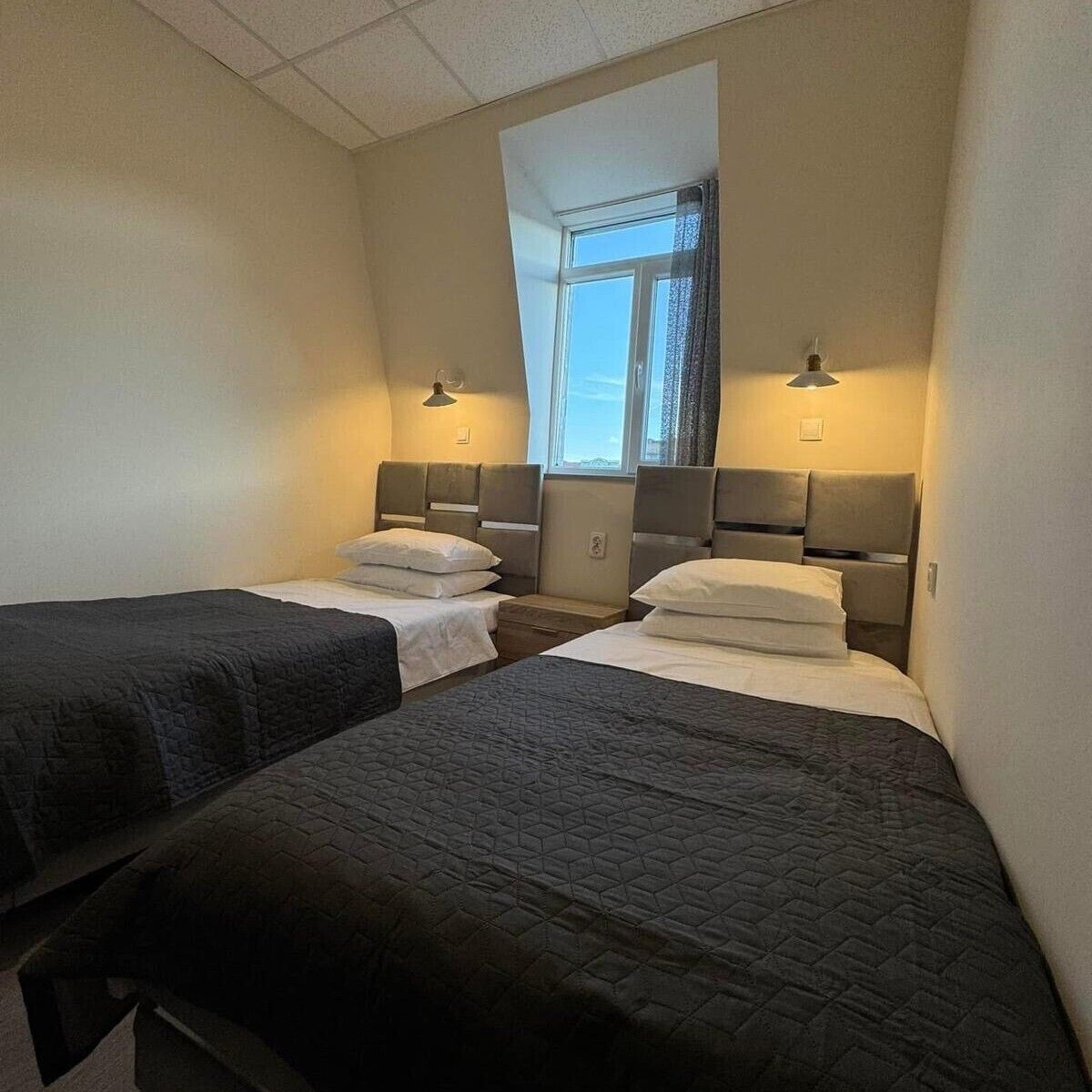 Quarto de hotel com duas camas de solteiro, cada uma com cabeceira e luminárias de cabeceira.